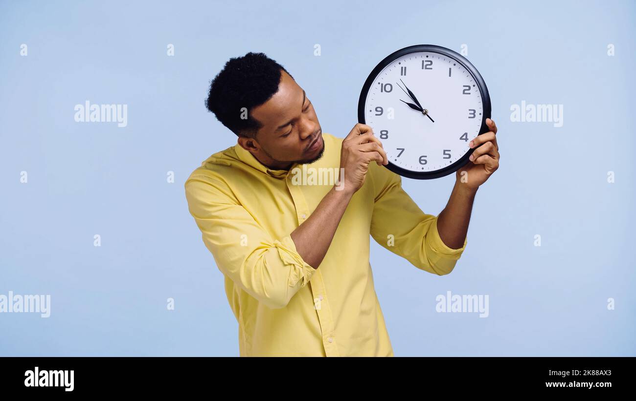 african american man in yellow shirt holding clock isolated on blue ...