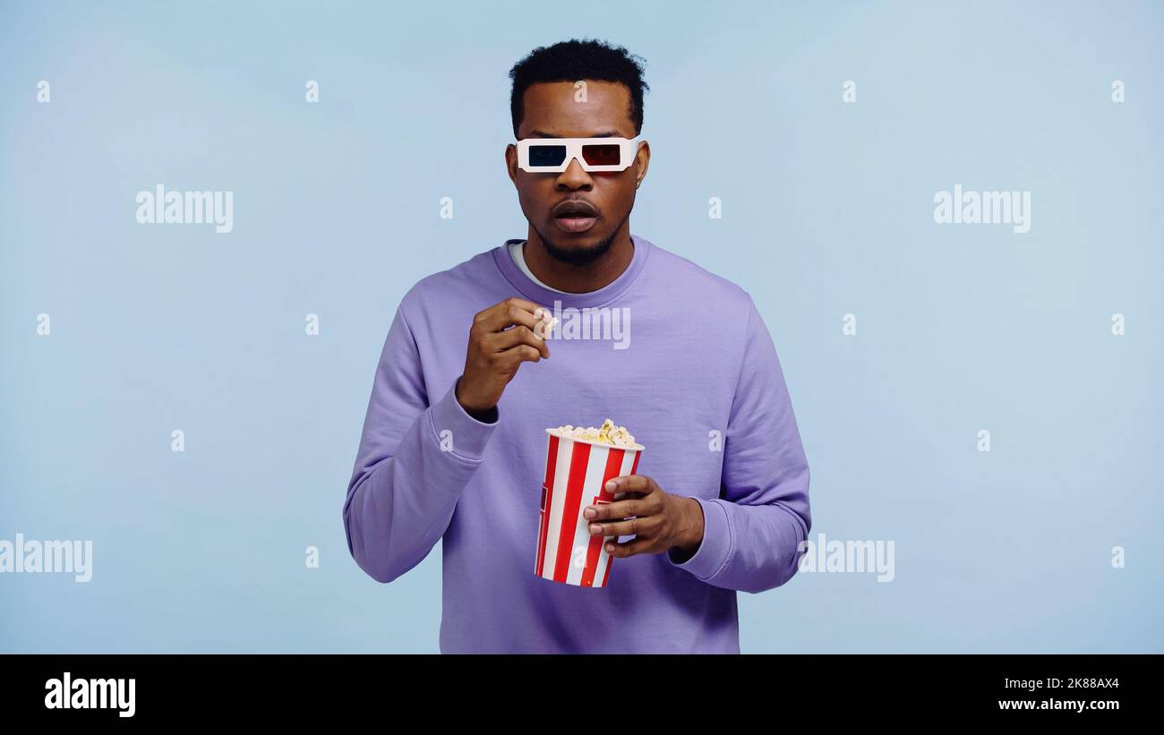 focused african american man in 3d glasses watching movie and holding popcorn bucket isolated on ...