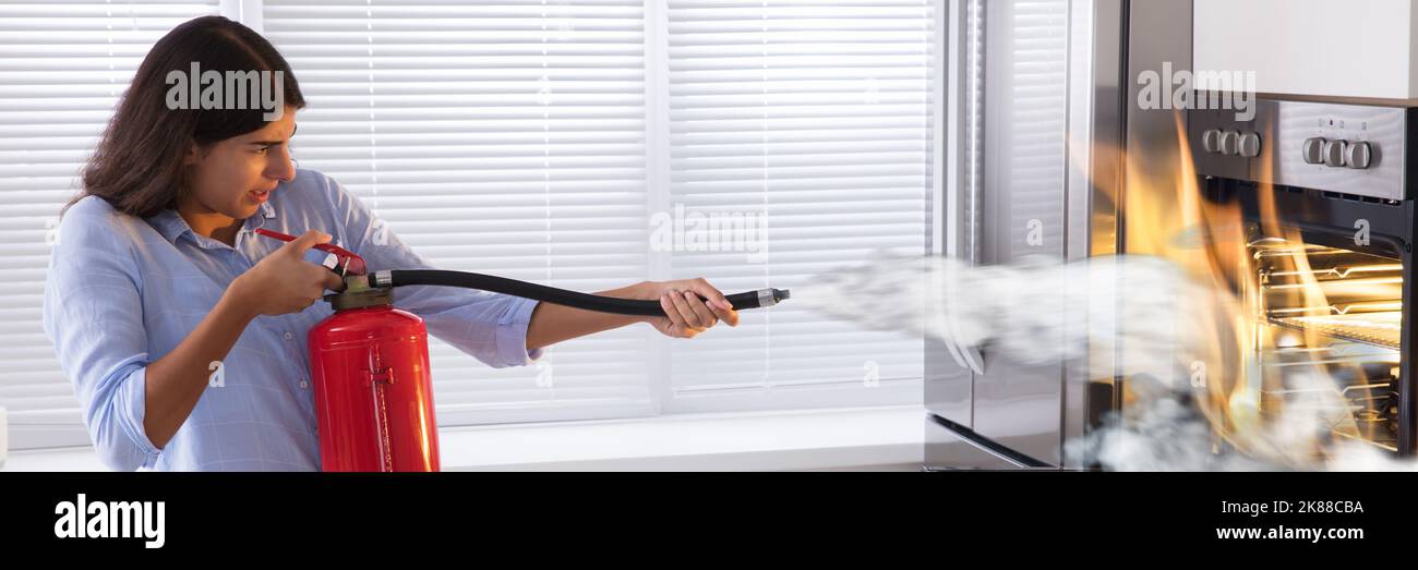 Woman Using Fire Extinguisher In Kitchen. Home Disaster Stock Photo - Alamy