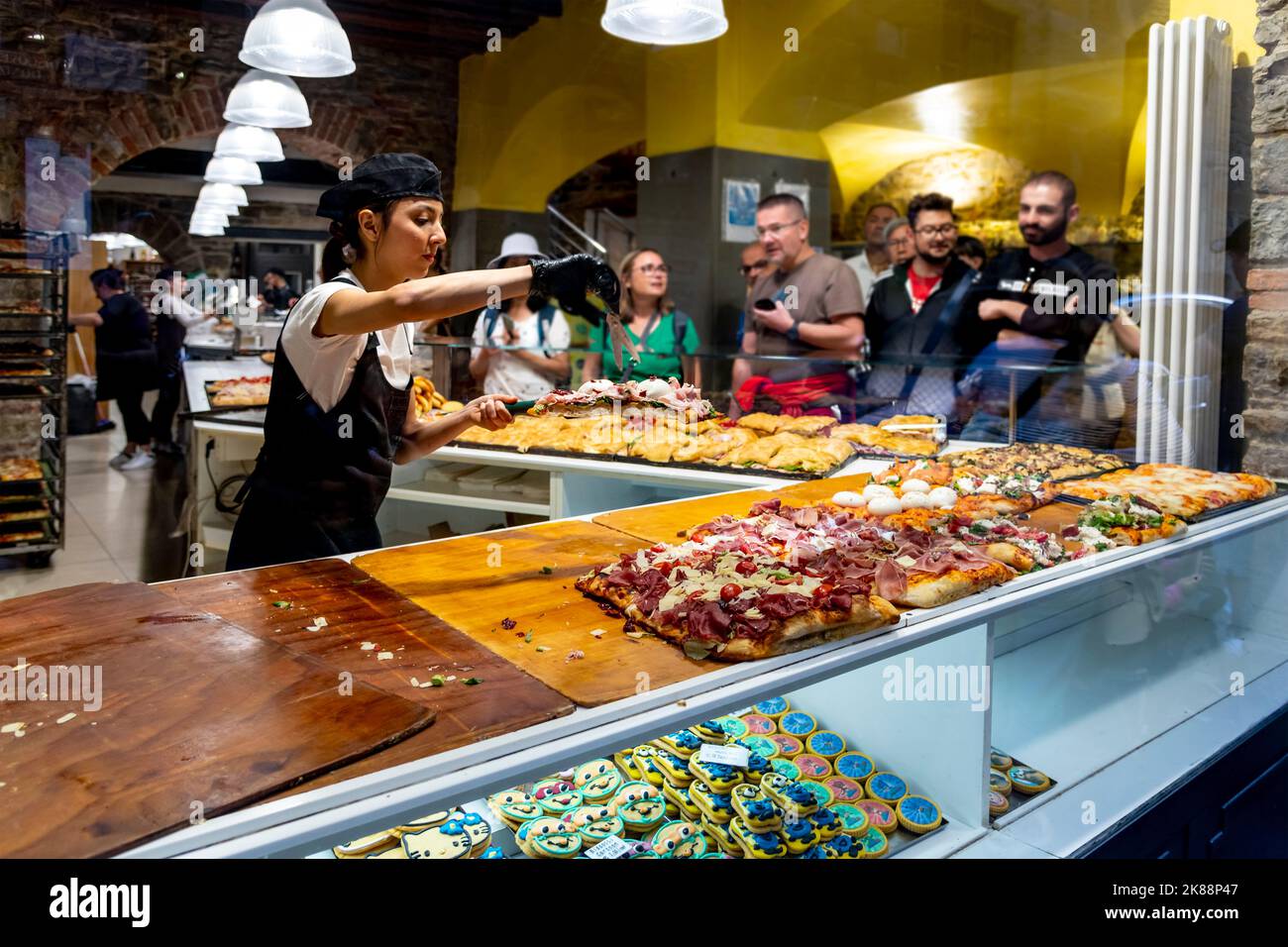 A female restaurant worker slices pizza slices for customers behind a ...