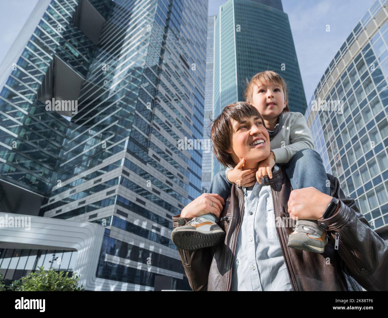 Little boy sits on father's shoulders between skyscrapers. Dad and son ...