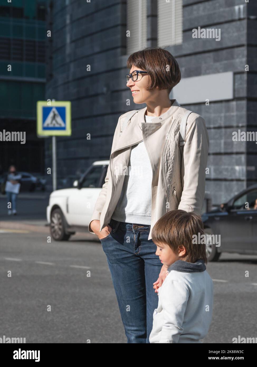Mother and son stand on street in sunlight. Woman and kid in modern ...