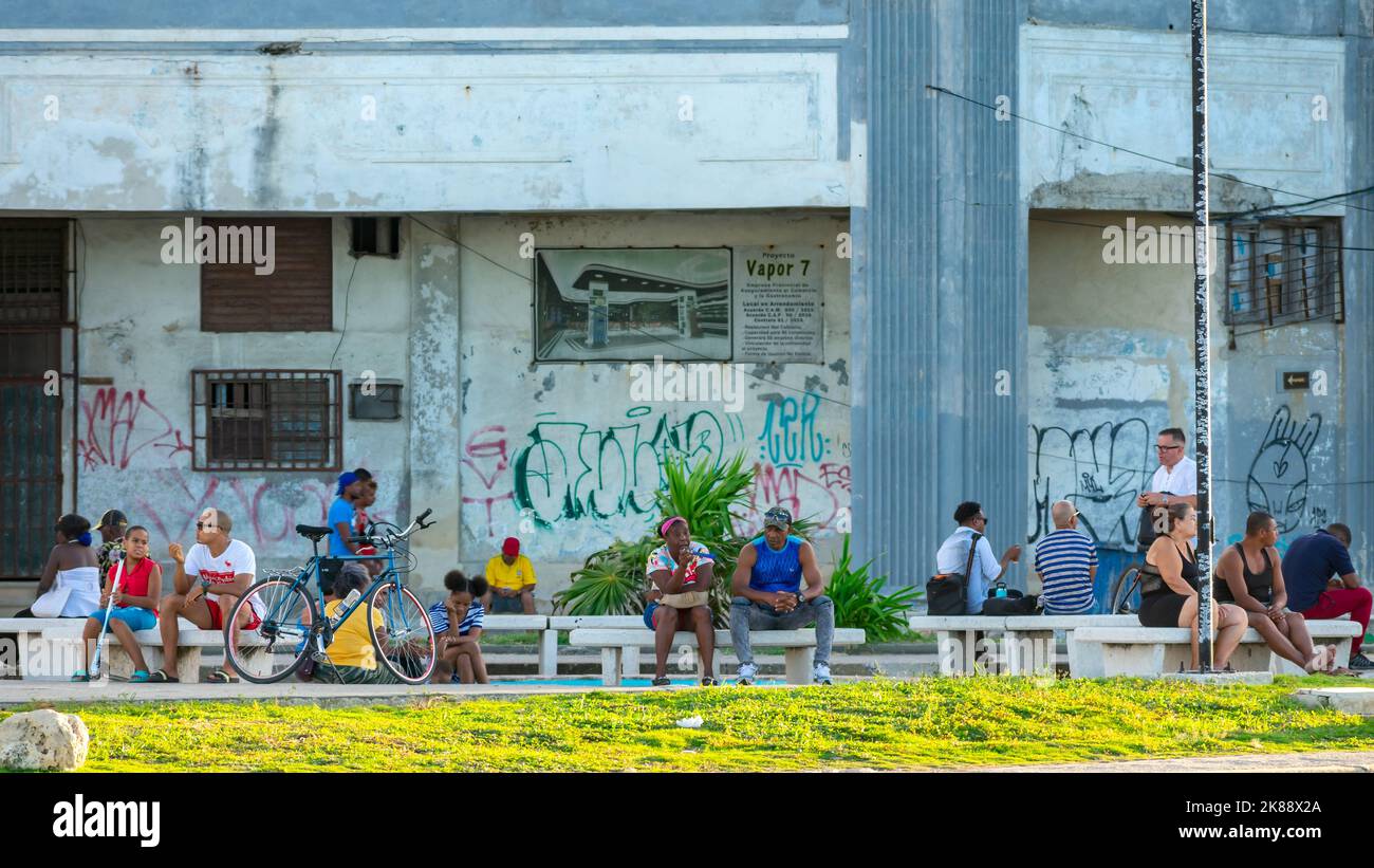 Group of Cuban people sitting by an old building covered in tagging ...
