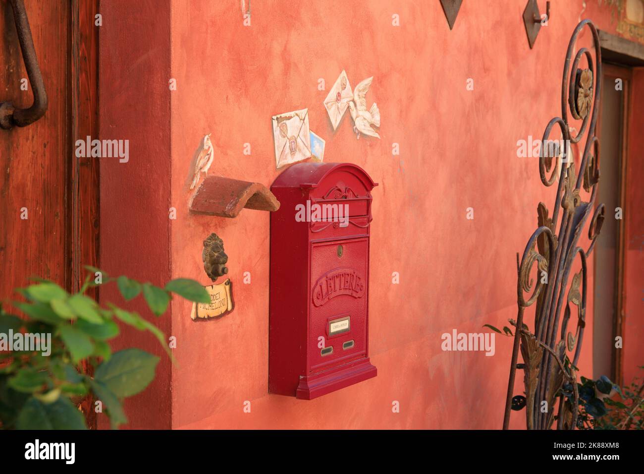 A red Italian mailbox on a red wall with a decorative wrought iron ...