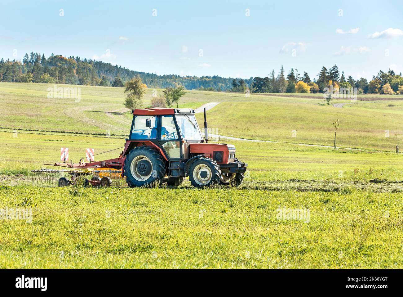 Red tractor turning cut grass to dry for hay in Czech Republic ...