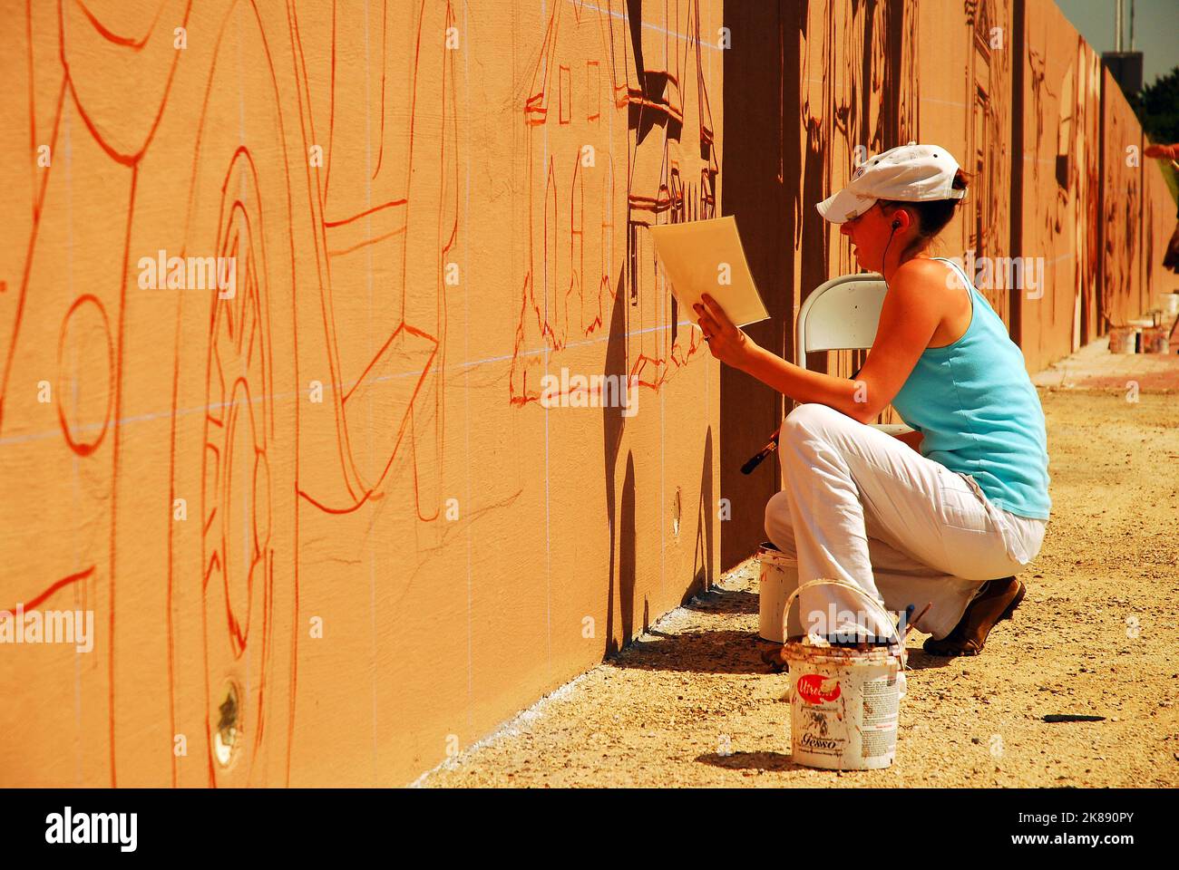 A young woman paints a mural on the walls on the perimeter of ...