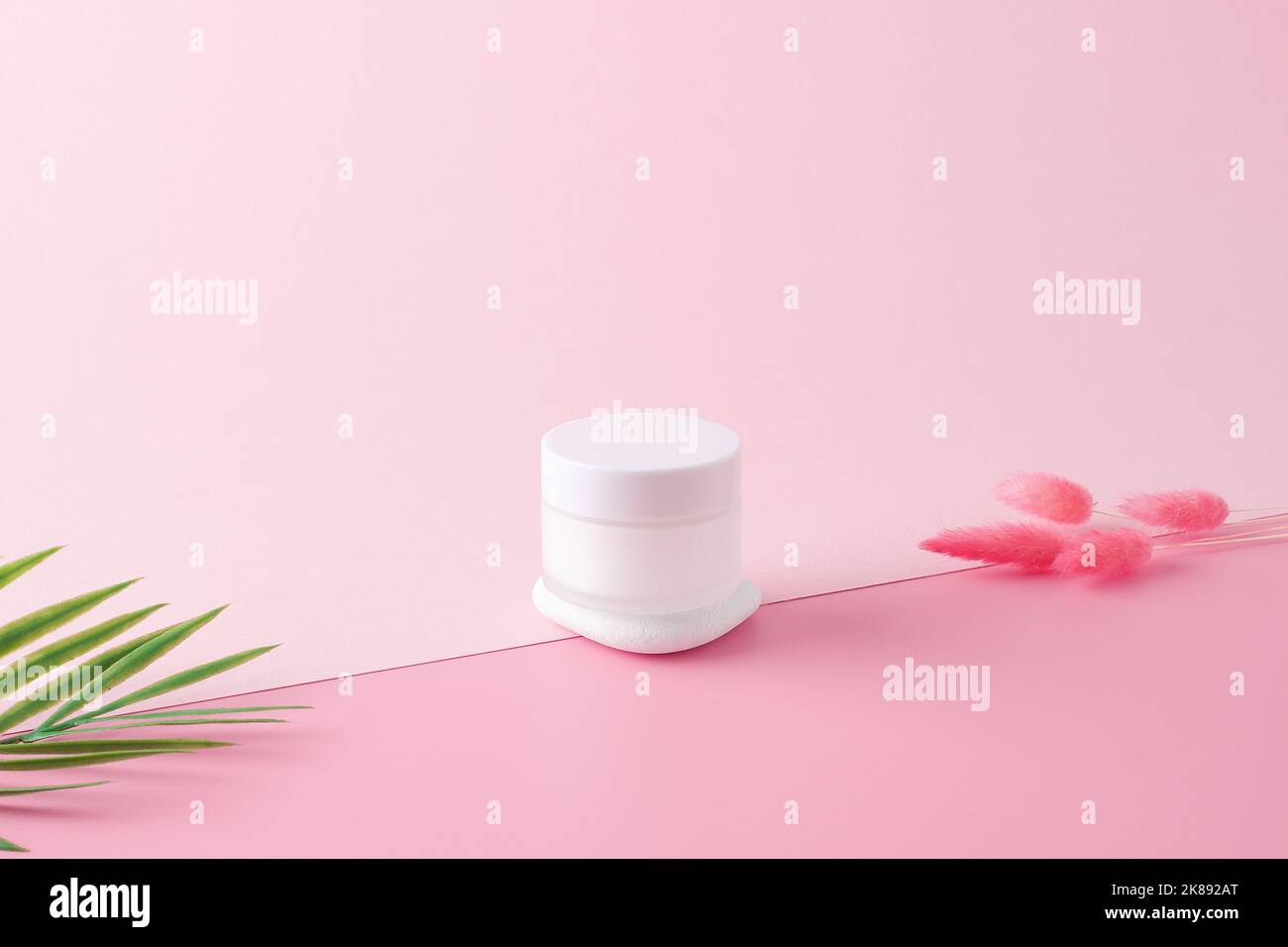 Jar of cosmetic cream with flowers and stone on pink background. Close ...