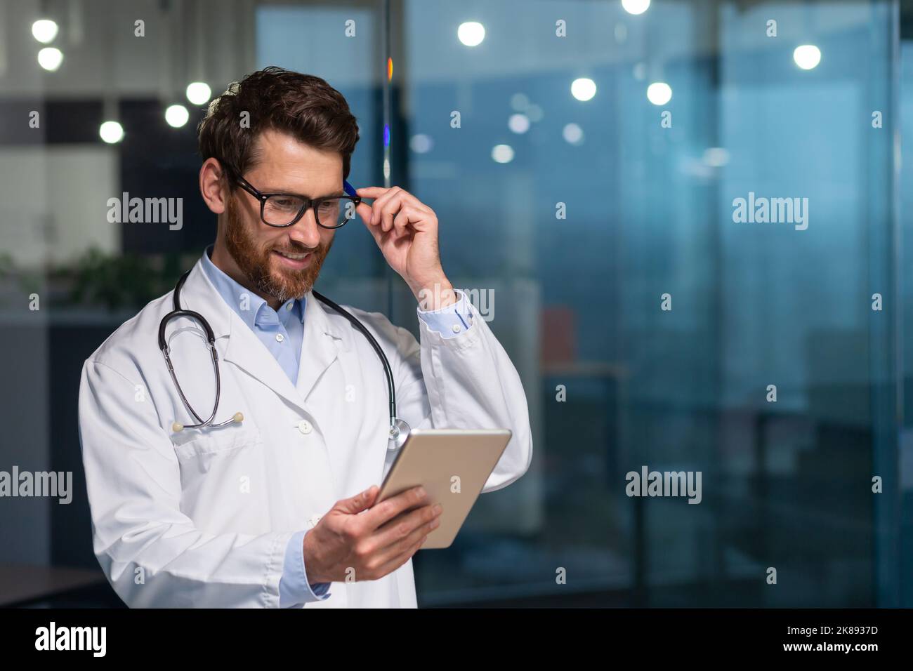 Cheerful and smiling senior doctor in glasses and medical gown reading ...