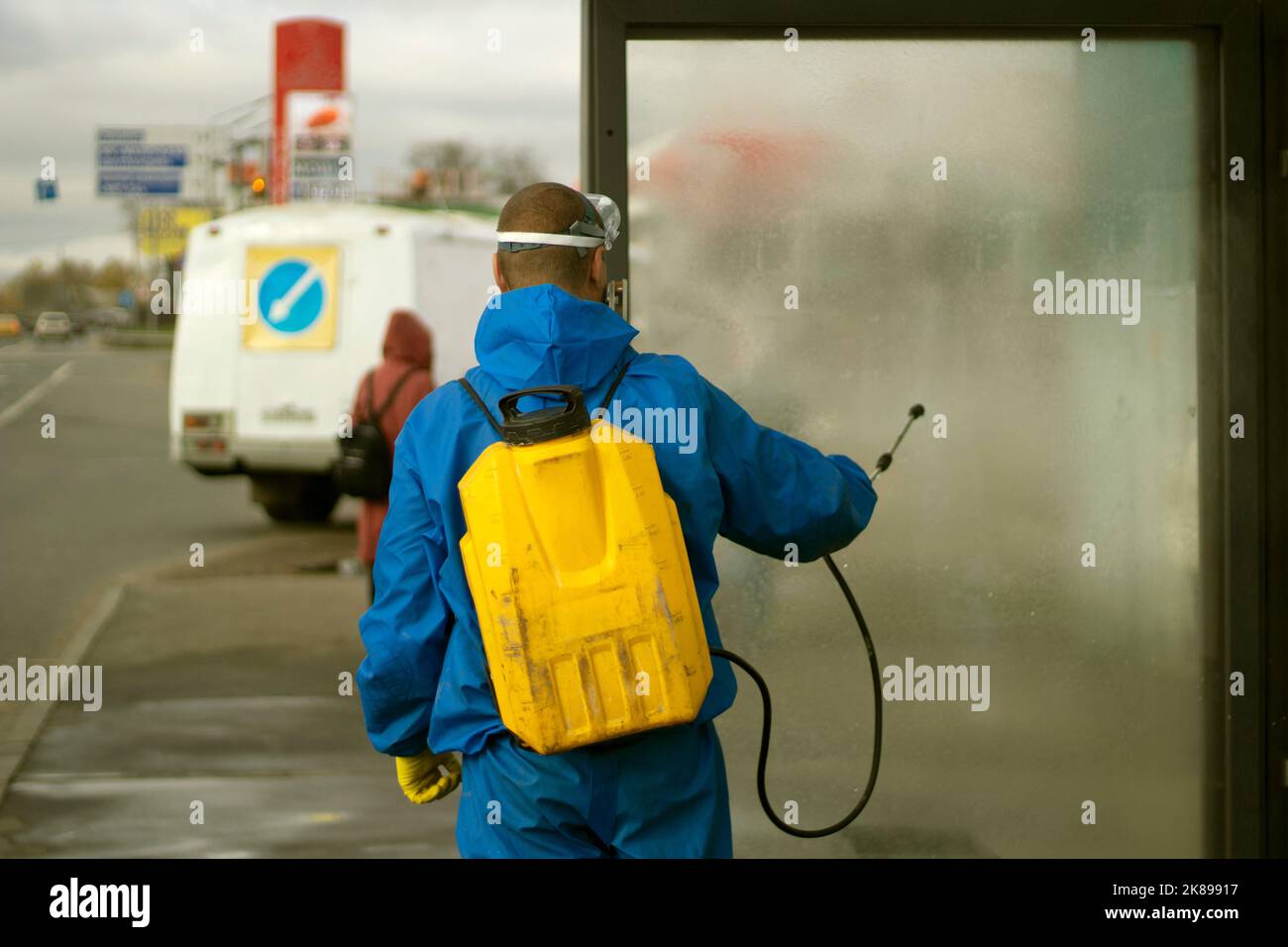 Guy washes bus stop. Worker with canister of water. Spraying detergent ...