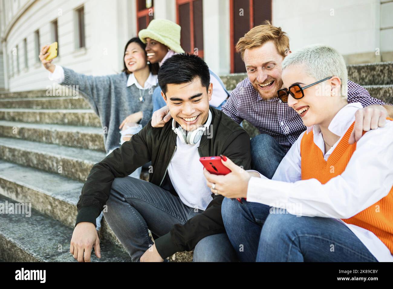 Group of multiracial young friends sitting together outdoors using ...