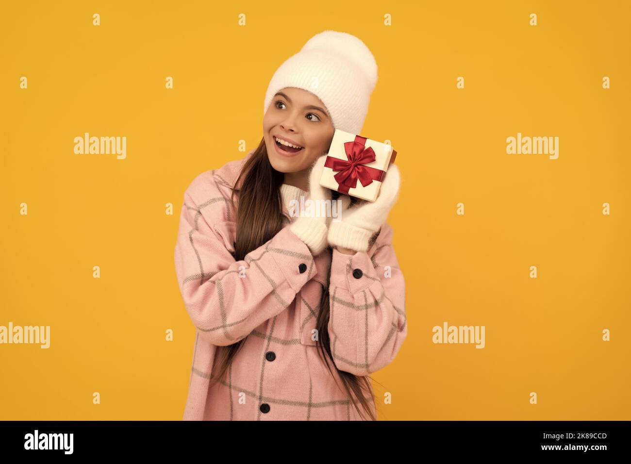 curious kid in hat and mittens hold gift box on yellow background, new ...