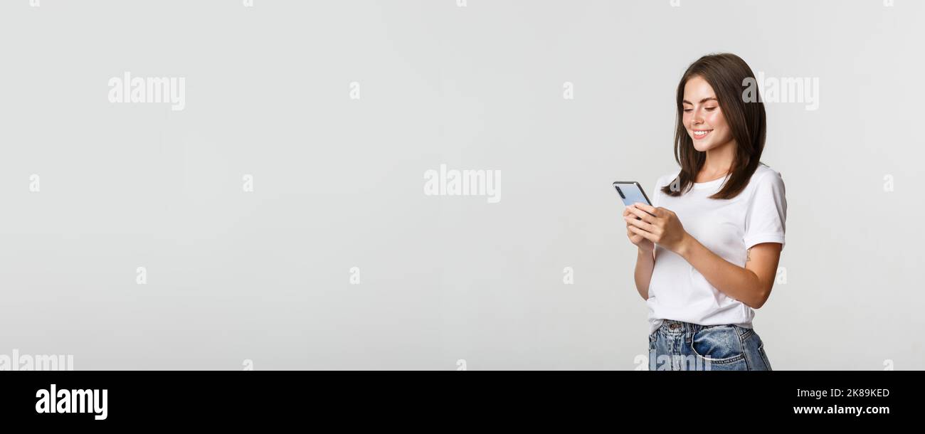 Beautiful smiling girl using mobile phone, looking at smartphone ...