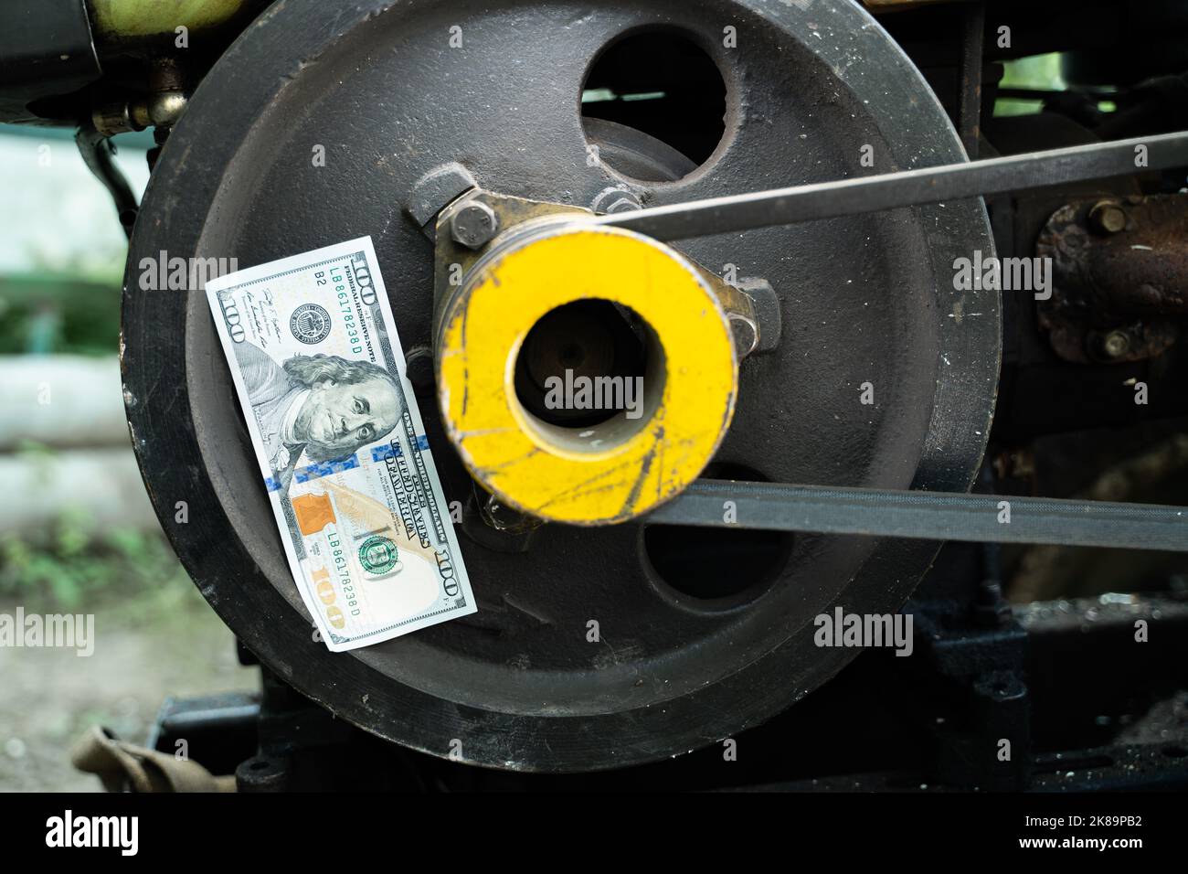 A hundred dollar bill stuck to a tractor pulley close-up. Money and the ...