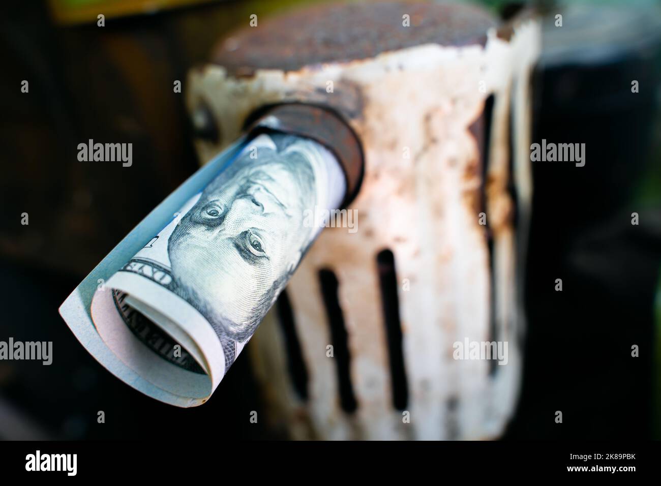 A hundred dollar bill covers the exhaust pipe of a mini tractor. Money ...