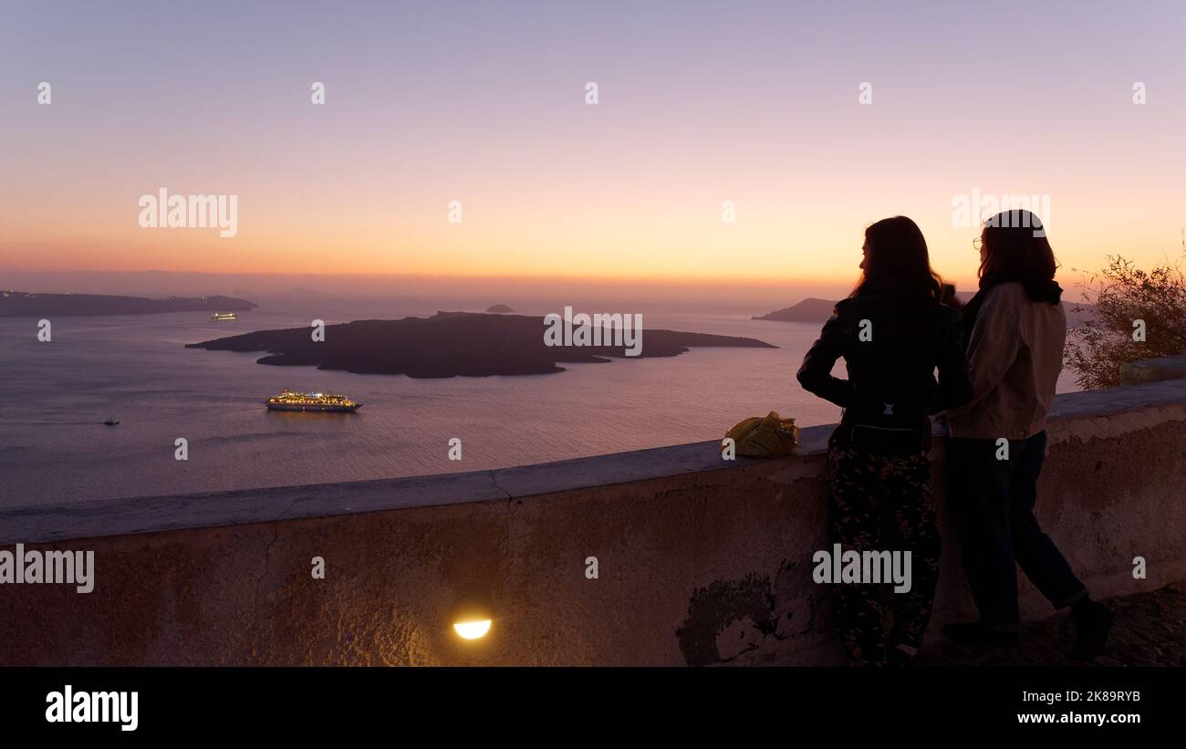 Two women enjoy the Sunset over Thirasia island from a a coastal path ...