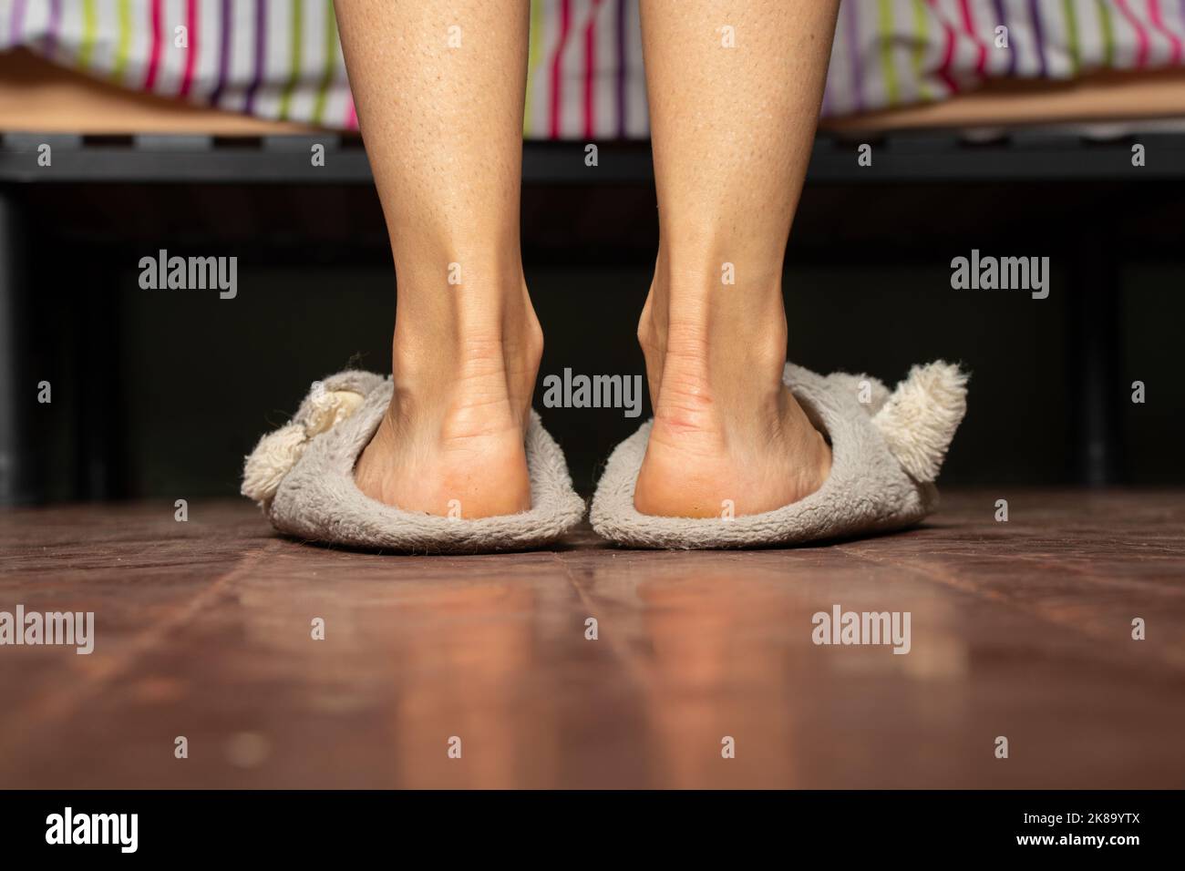 girl's feet in indoor slippers on the wooden floor near the bed, feet ...