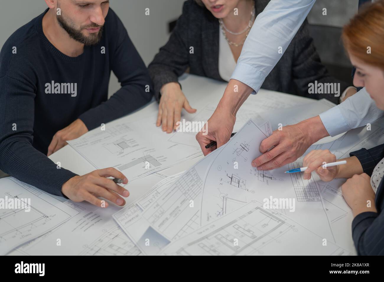 Close-up of the hands of four colleagues with blueprints on the table ...
