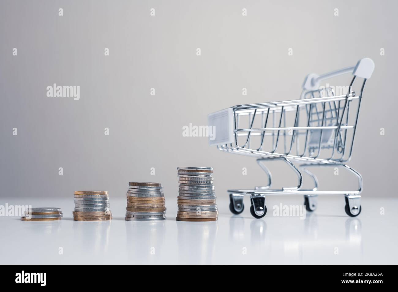 Shopping cart With Stacked Coins On white Desk. Miniature Shopping cart ...