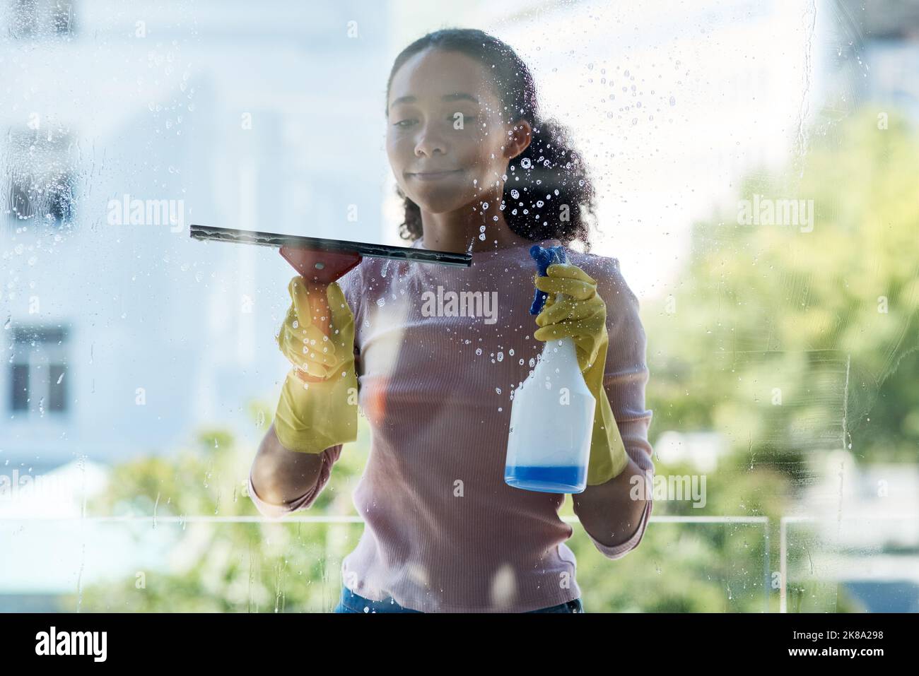 Time to walk into some windows. a young woman cleaning her window at ...