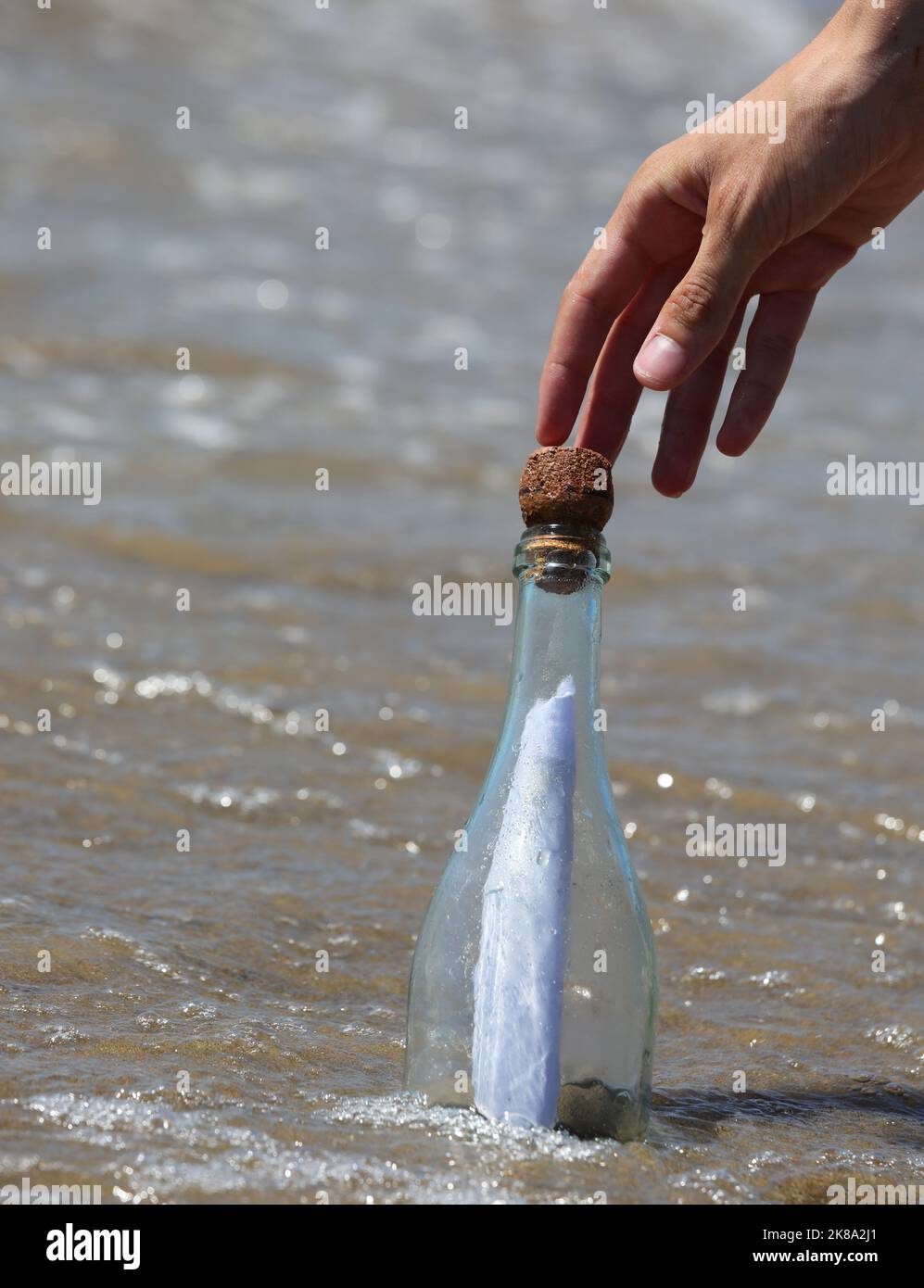 hand and secret message in the transparent glass bottle on the shore ...