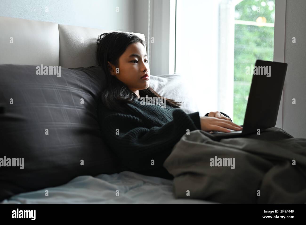 Bored teenager girl lying on bed and watching movie on laptop in ...