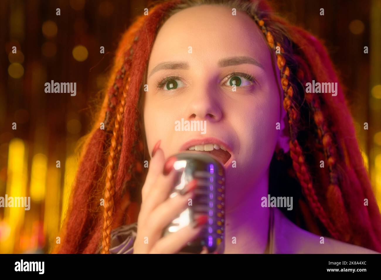 Young woman with ginger dreadlocks singing into microphone. Portrait of female singer with ...