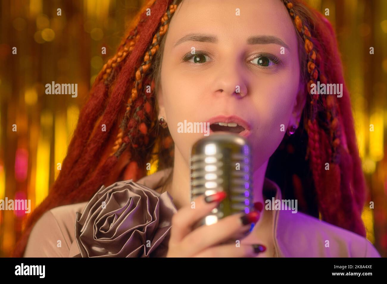 Young woman with ginger dreadlocks singing into microphone. Portrait of female singer with ...