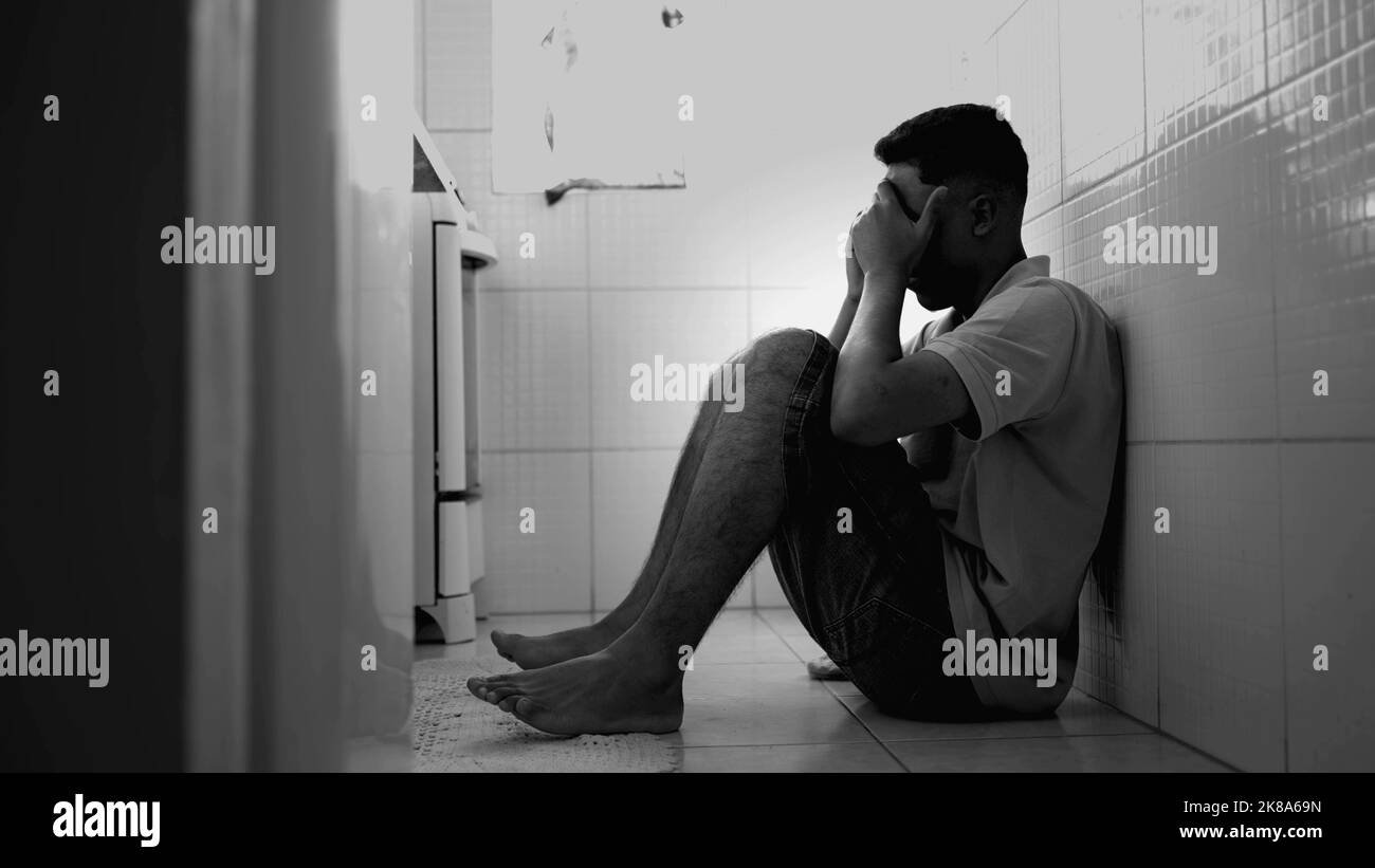 Depressed young man covering face sitting on kitchen floor during hard ...