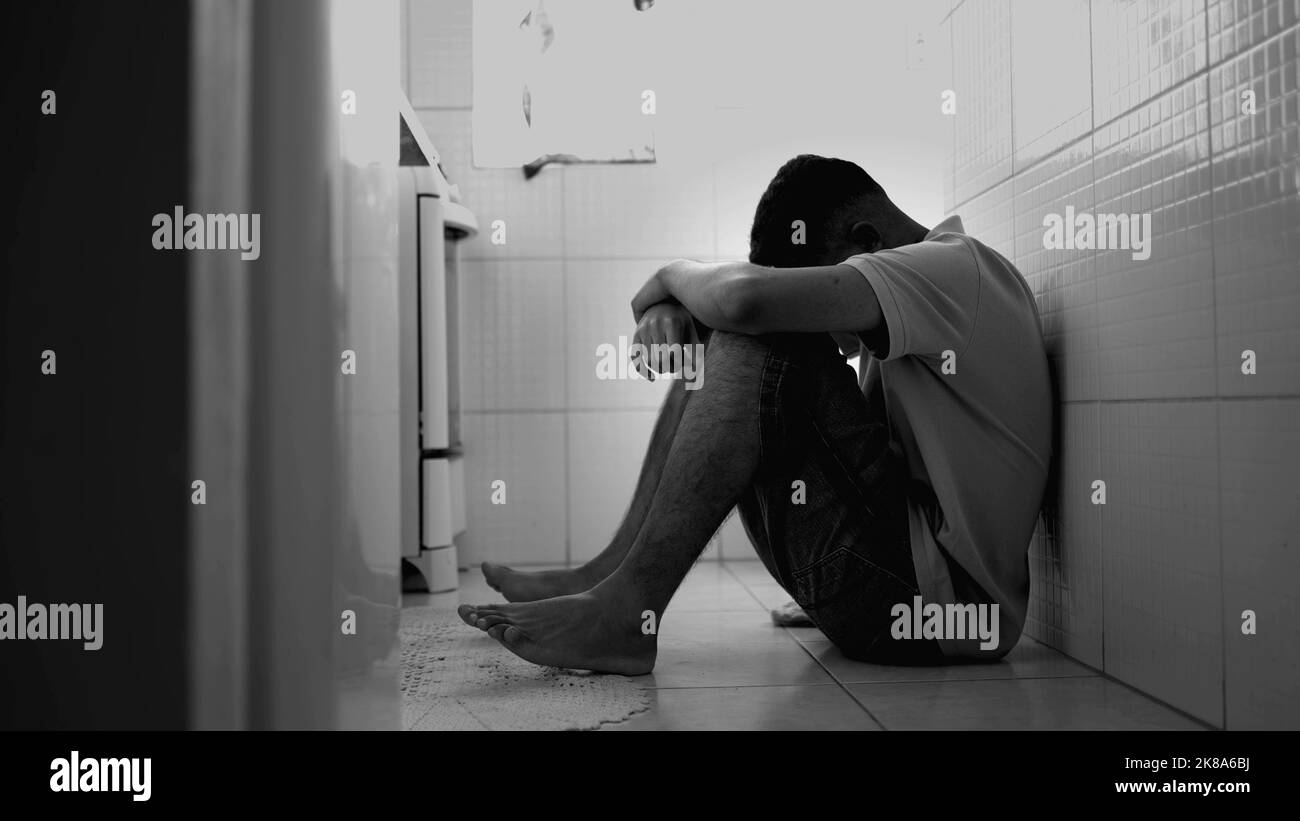 Depressed young man covering face sitting on kitchen floor during hard ...