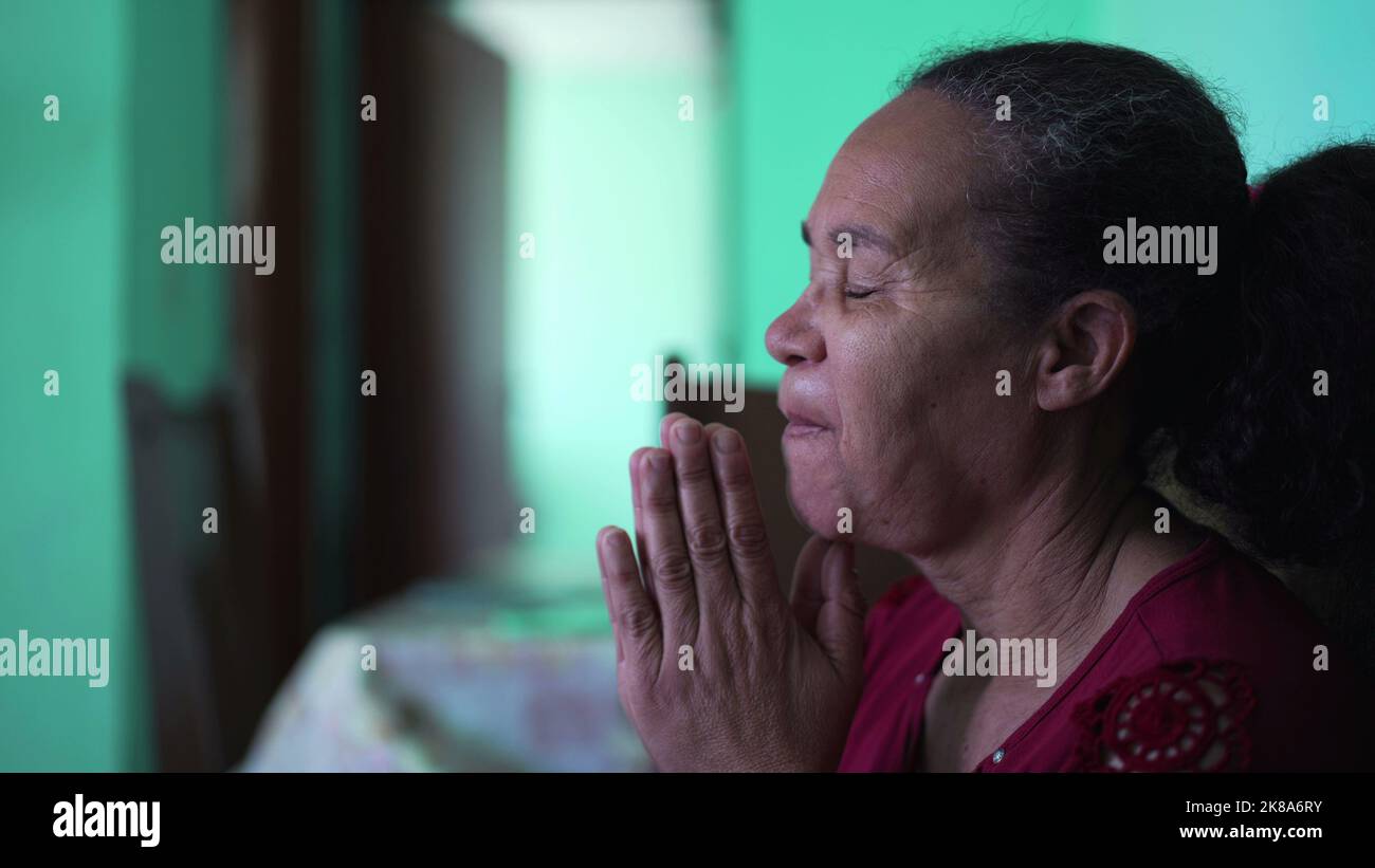 Mature senior woman praying to God at home. An older latin person ...