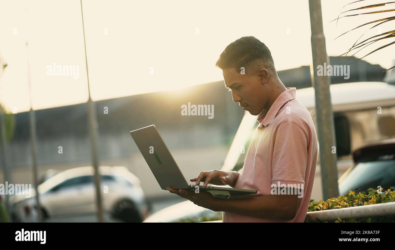 A young hispanic guy studying in front of computer stands outdoors in ...