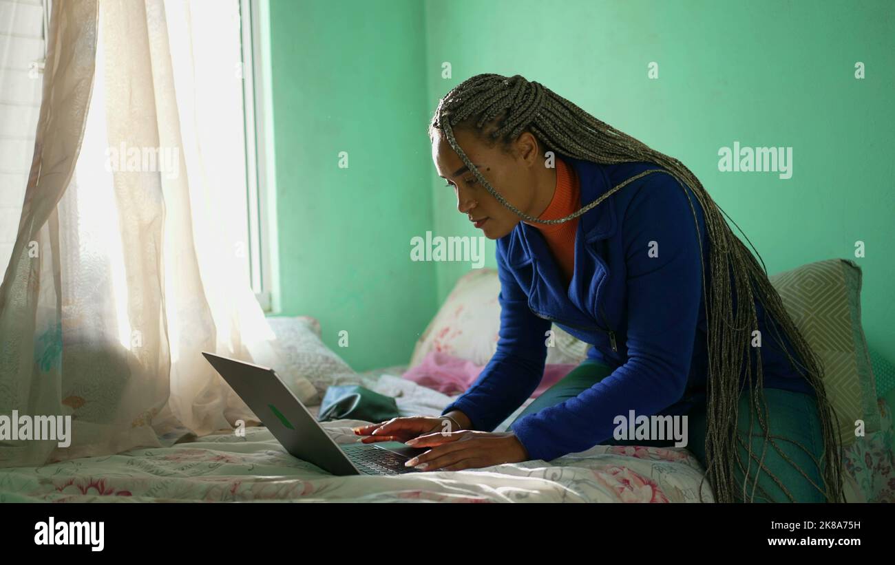 African American young woman sitting in bed turning laptop ON. A black ...