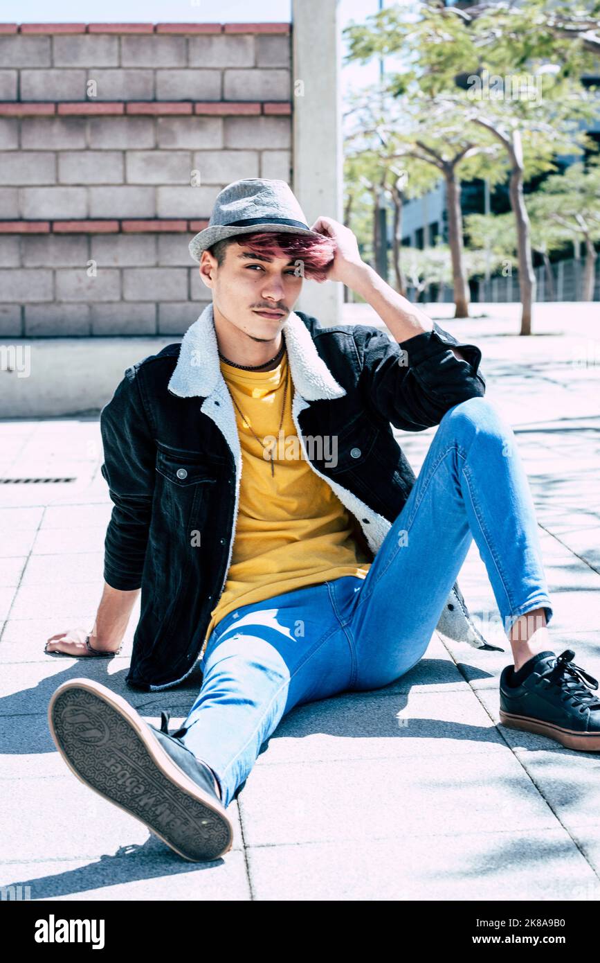 One modern trendy boy teenager sitting on the ground in the urban town ...