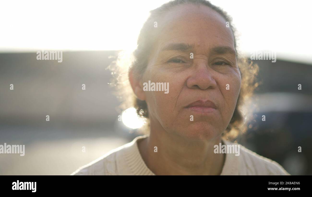 One mature hispanic woman stands outdoors with serious emotion. South ...