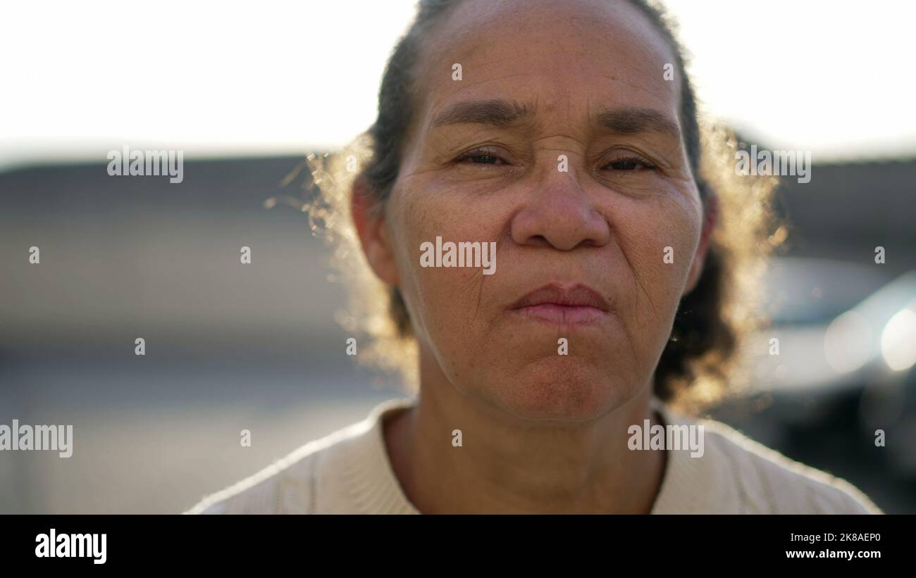 One mature hispanic woman stands outdoors with serious emotion. South ...
