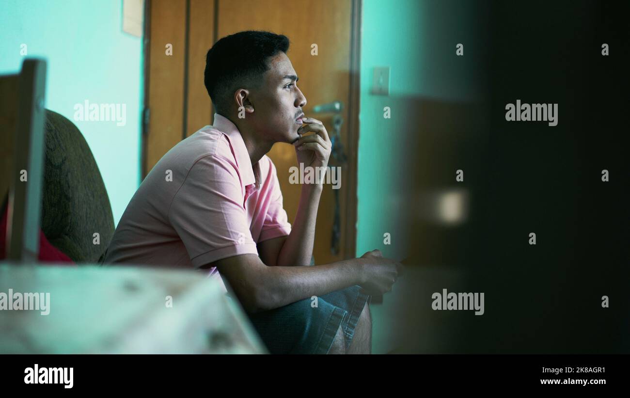 Person sitting at home pondering solution alone. A young Brazilian man ...