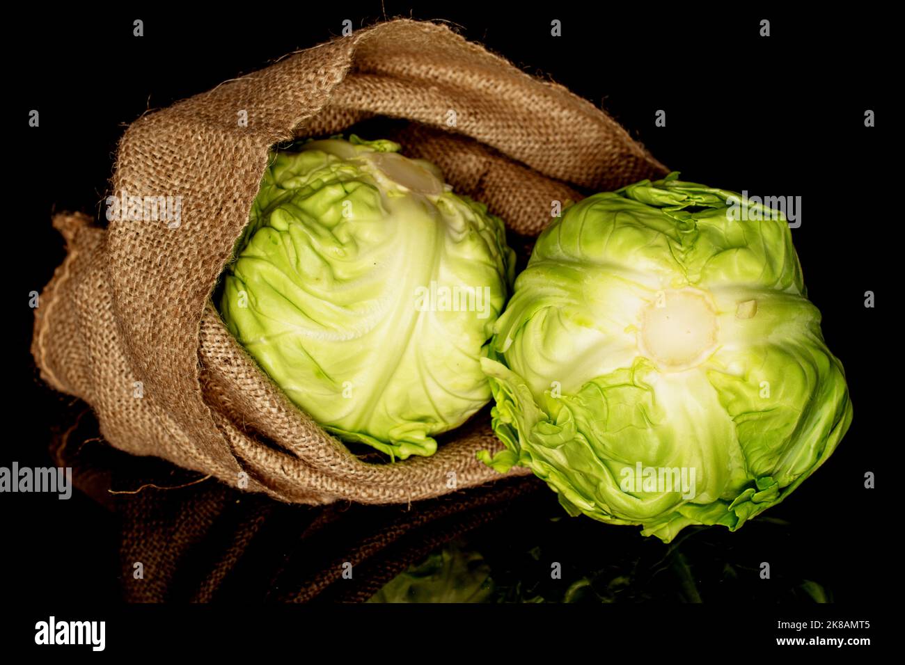 Two heads of fresh cabbage in a jute sack, macro, isolated on black ...