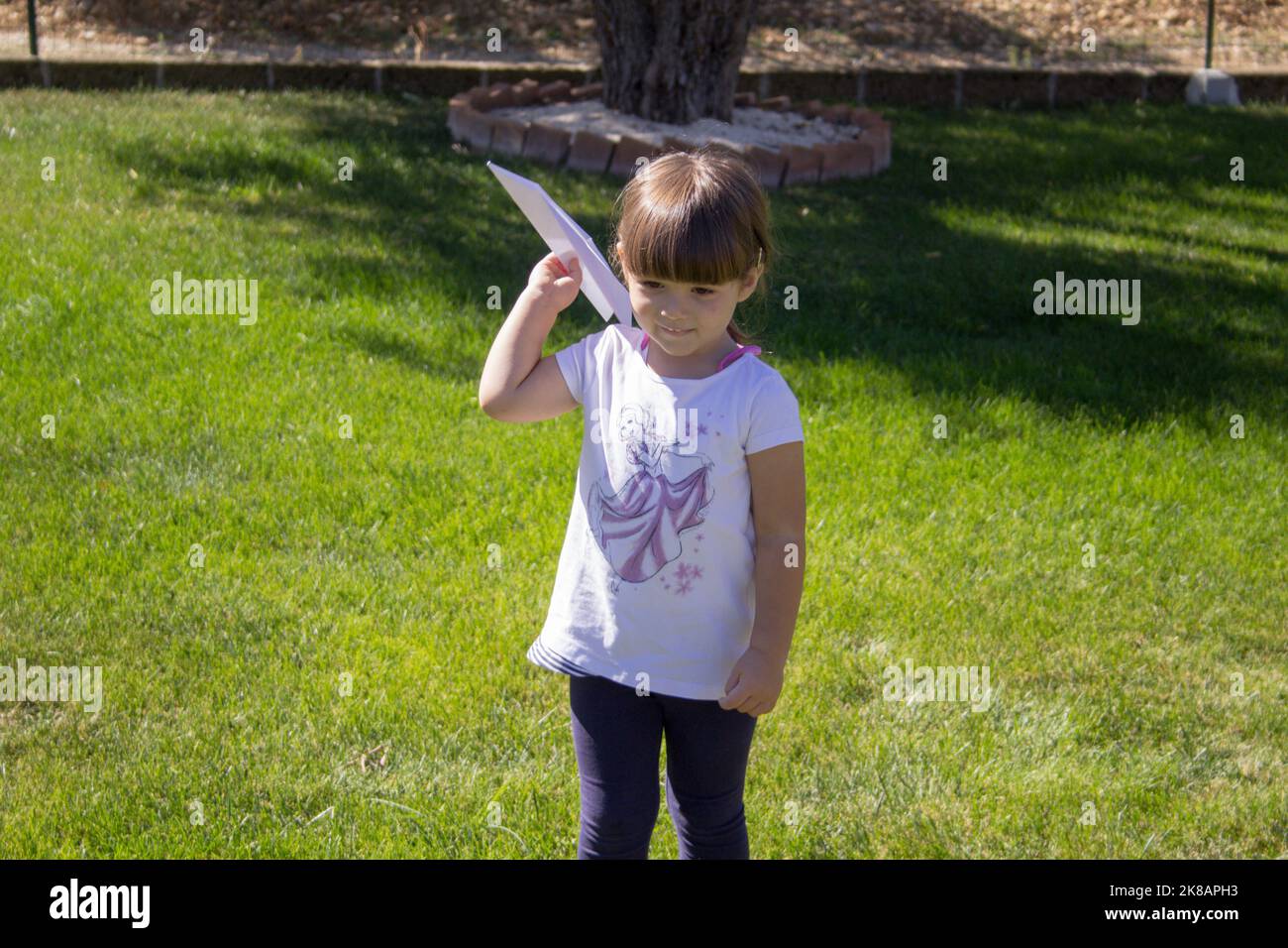 Adorable little girl playing to fly a paper plane in the garden at home ...