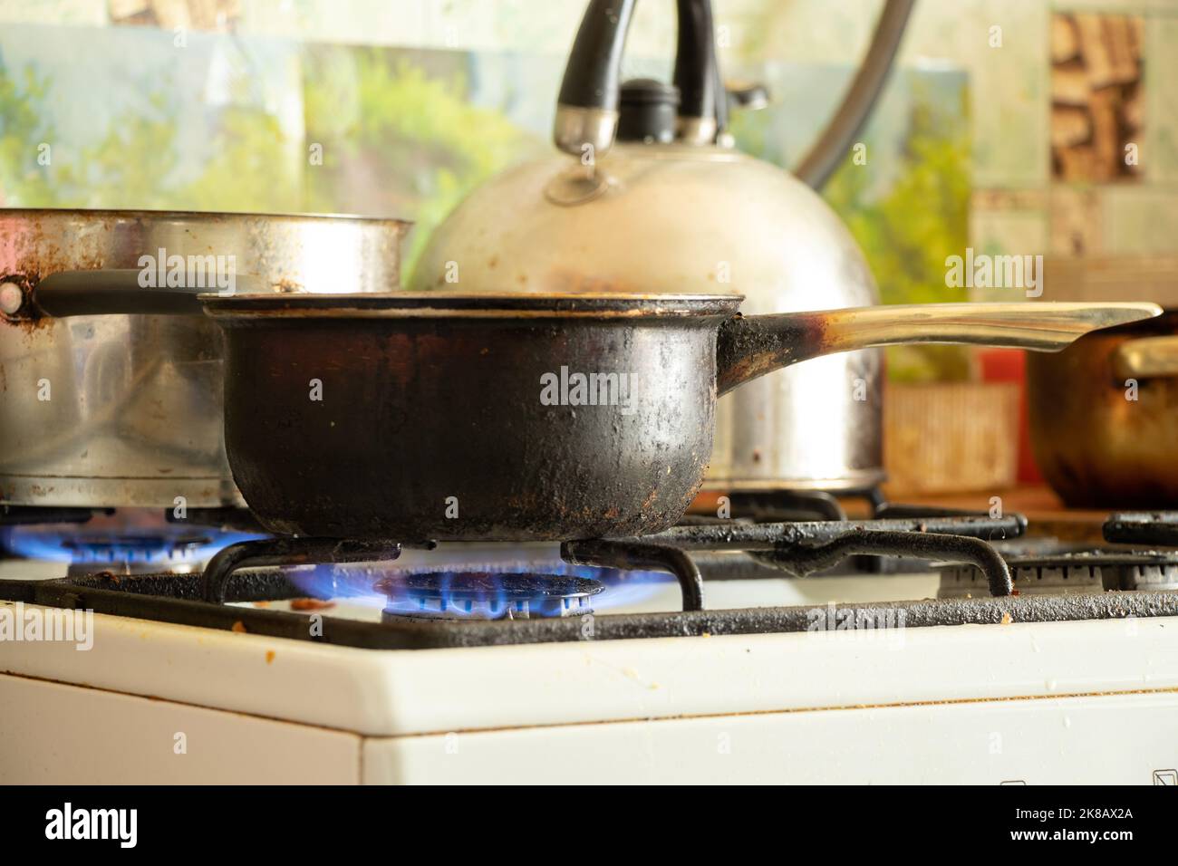a dirty saucepan stands on a dirty gas stove in the kitchen at home ...
