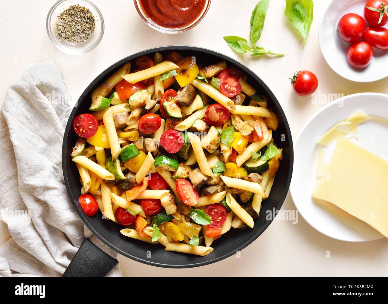 Penne pasta with roasted vegetables in cooking pan over light stone ...