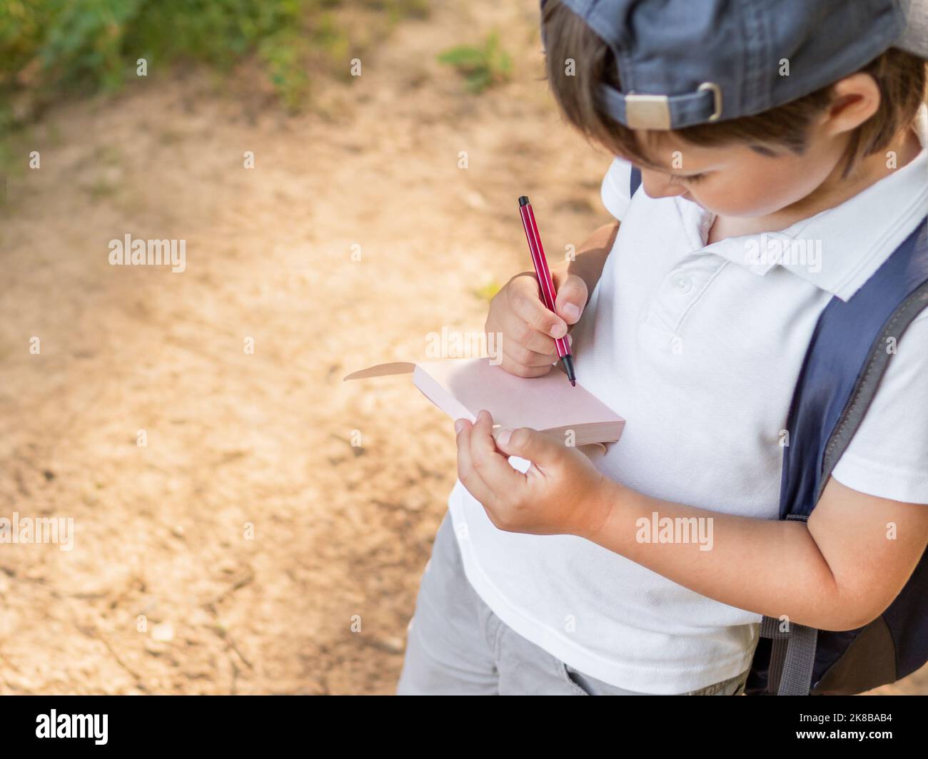 Mindful boy writes something in notebook while walking in forest ...