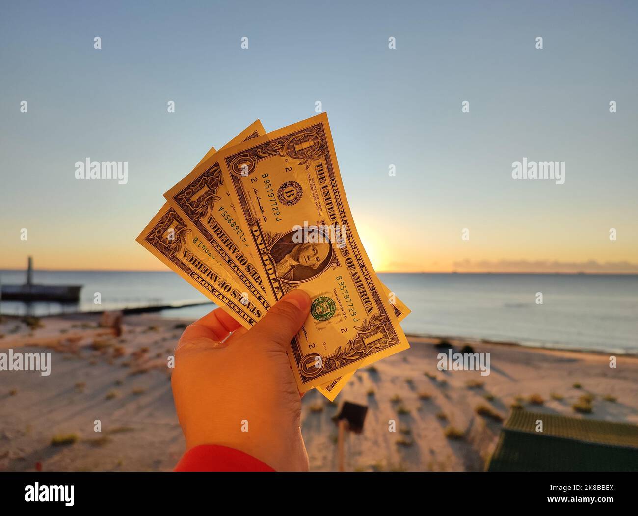 A man holding three one-dollar banknotes in his hand against backdrop ...