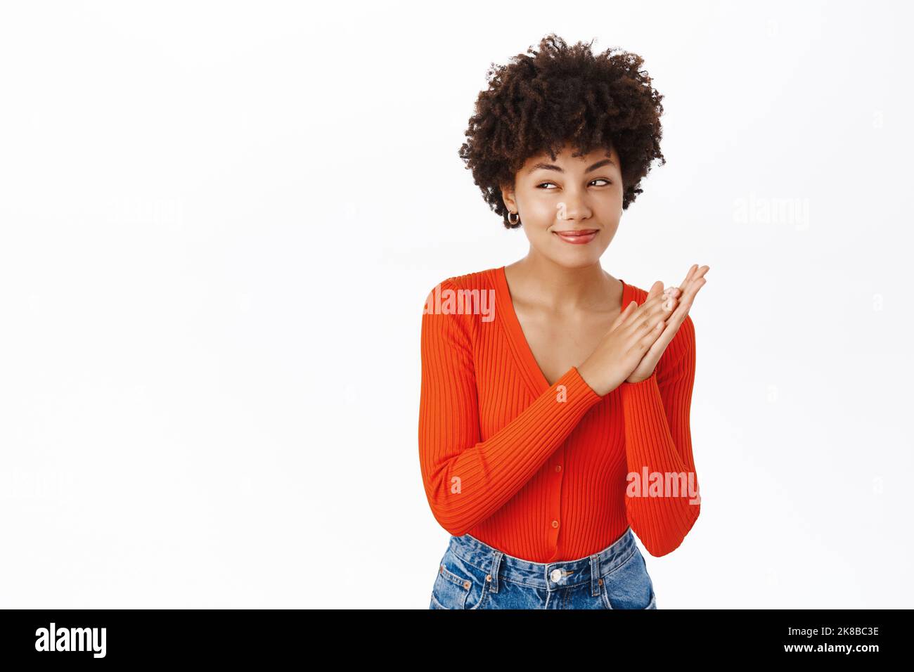 Smiling sly girl rubs her hands, thinks of smth, has plan, stands over ...