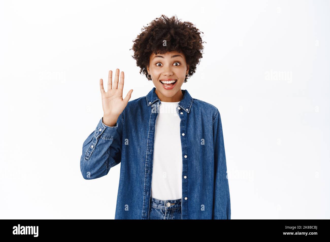 Friendly young modern girl say hi, waves hand and smiles happy, stands ...