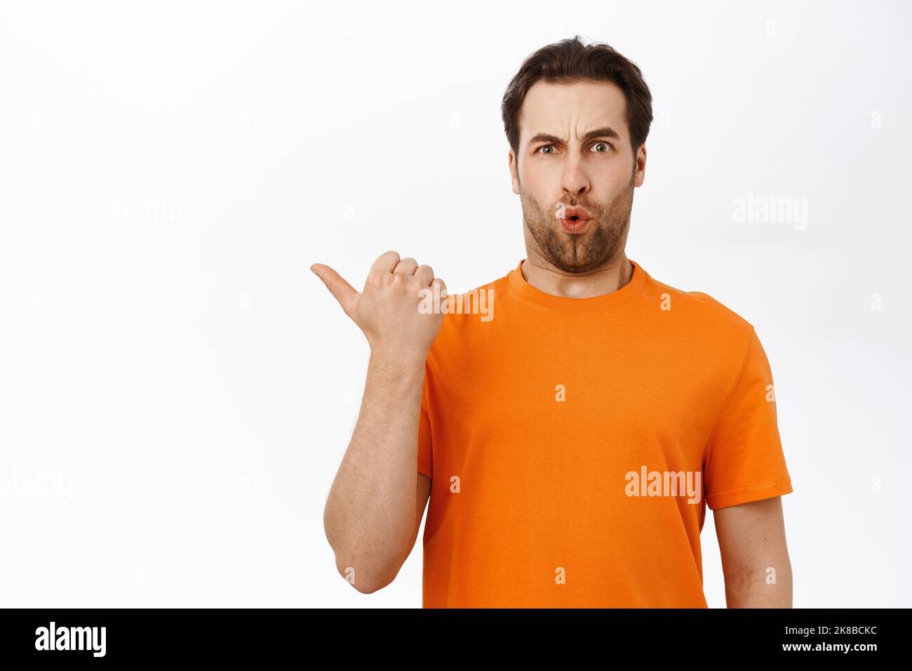 Confused man points left at smth strange. Guy in orange t-shirt shows ...