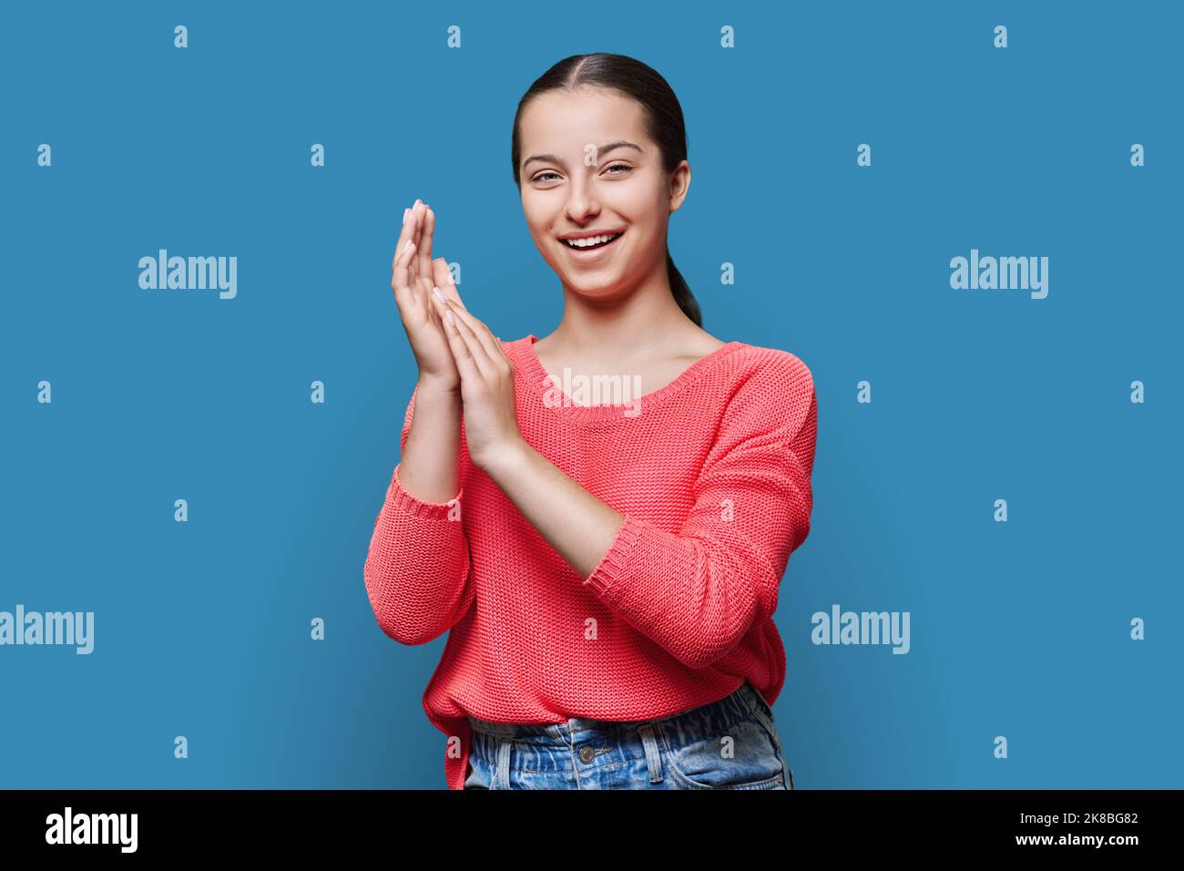 Young teenage girl clapping her hands on blue color studio background ...