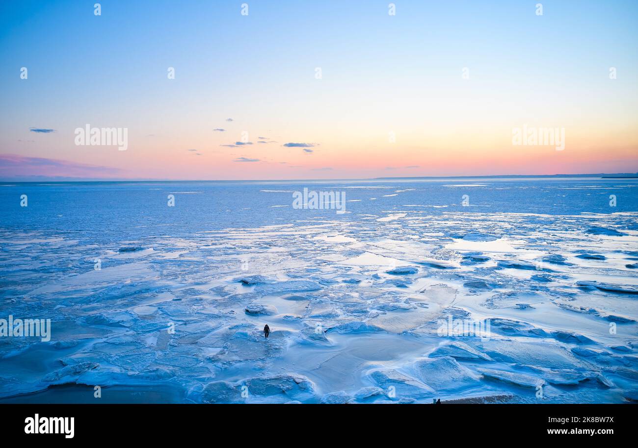 Aerial view - lonely man walk on ice on sunset over a frozen sea ...