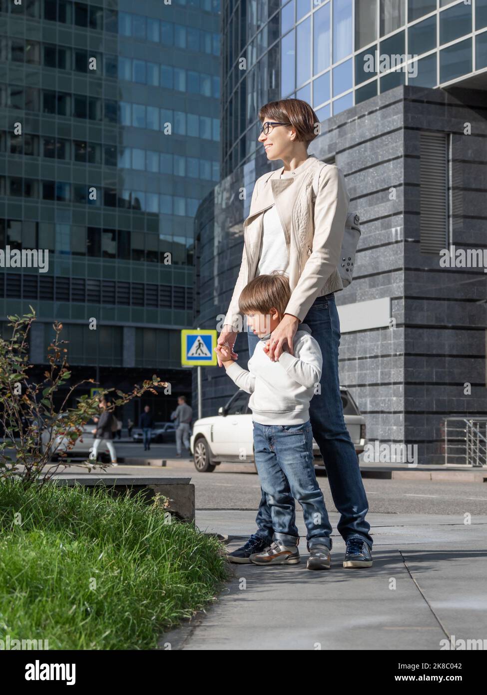 Mother and son stand on street in sunlight. Woman and kid in modern ...