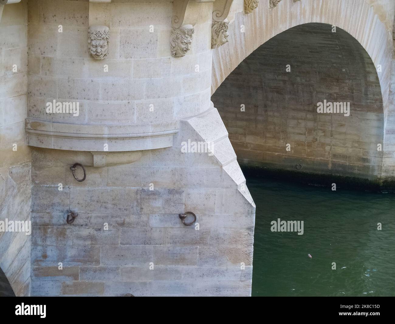River flowing under stone bridge with small gargoyle faces in Paris ...