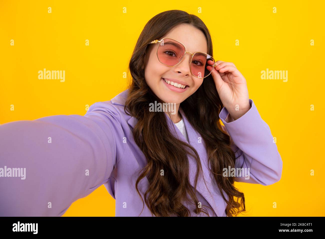 Trendy beautiful teenage model making selfie posing on yellow studio background. Teen fashion ...